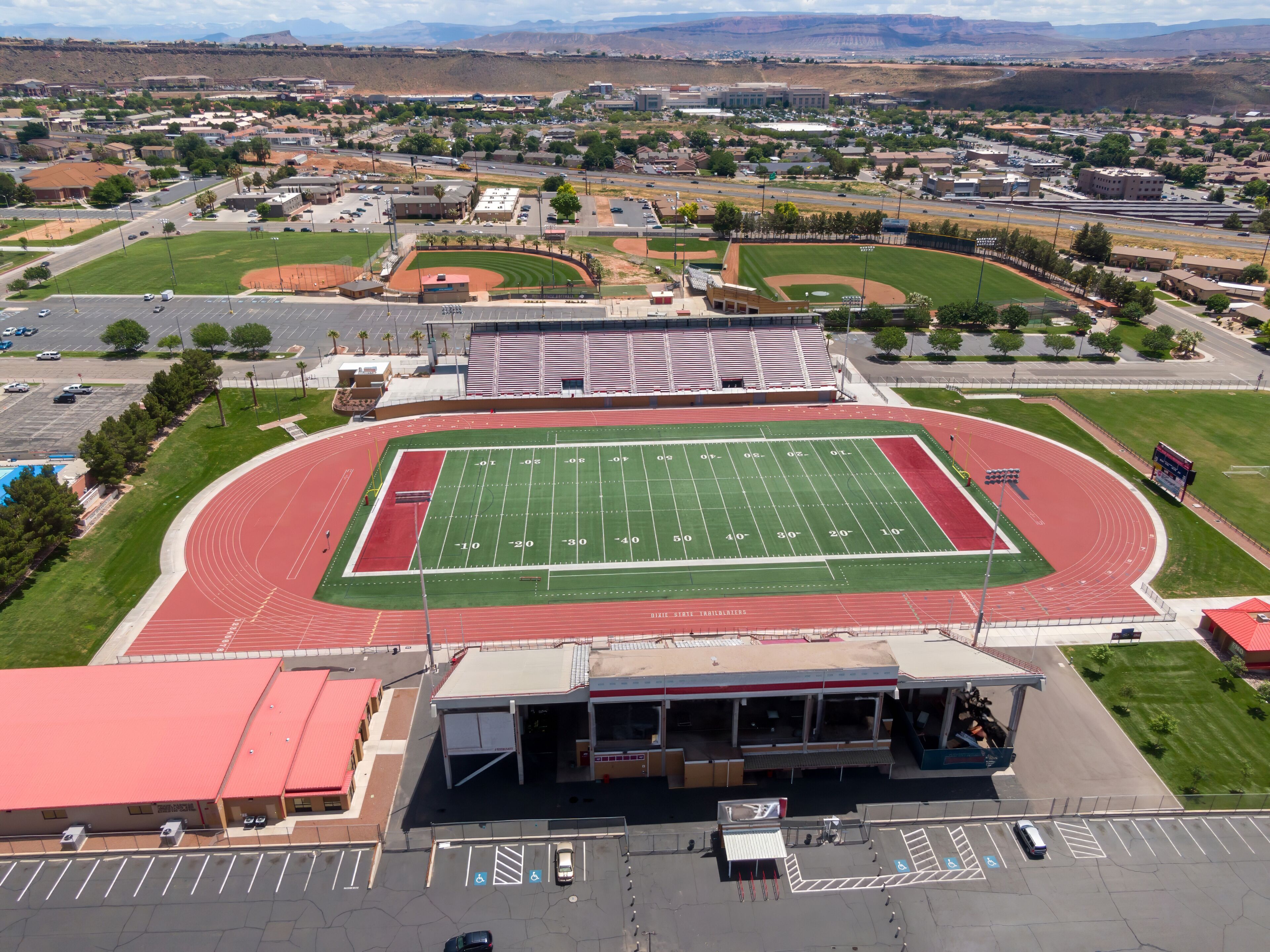 Um estádio grande com campo de futebol, estacionamento e edifícios ao redor.