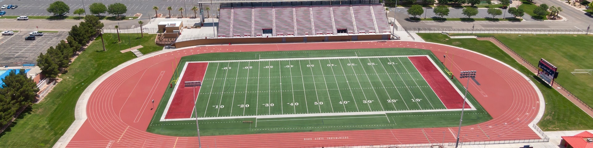 Um estádio grande com campo de futebol, estacionamento e edifícios ao redor.