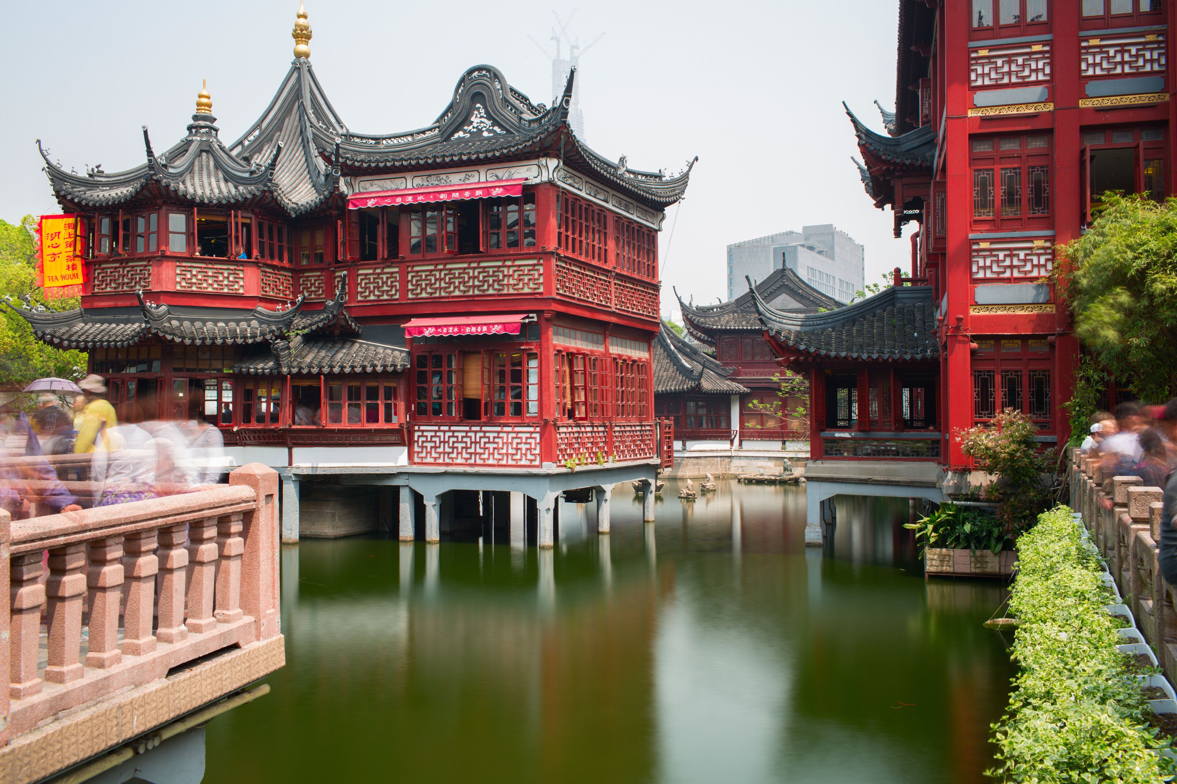 Arquitetura chinesa tradicional com cores vermelho e preto, um corpo d'água tranquilo e uma ponte.