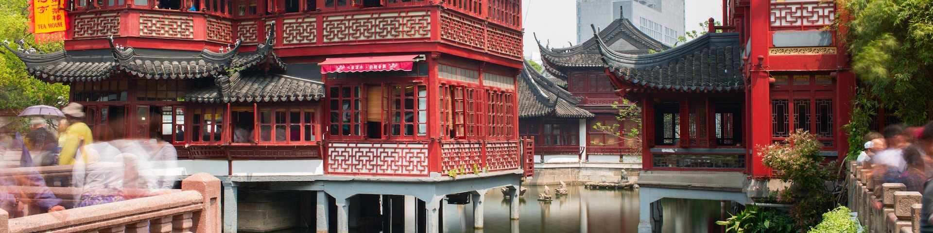 Arquitetura chinesa tradicional com cores vermelho e preto, um corpo d'água tranquilo e uma ponte.