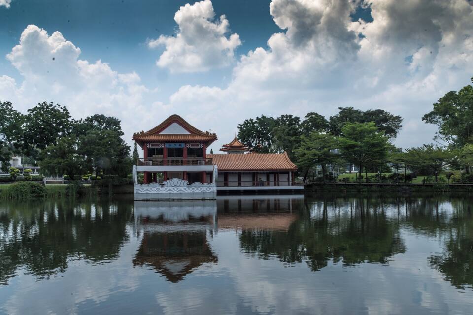 Um edifício tradicional chinês refletido na água, cercado por árvores e um céu limpo.