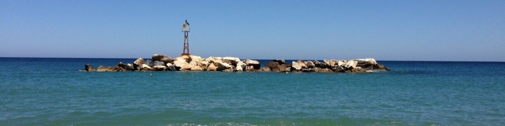 Um molhe rochoso com um farol ao longe.