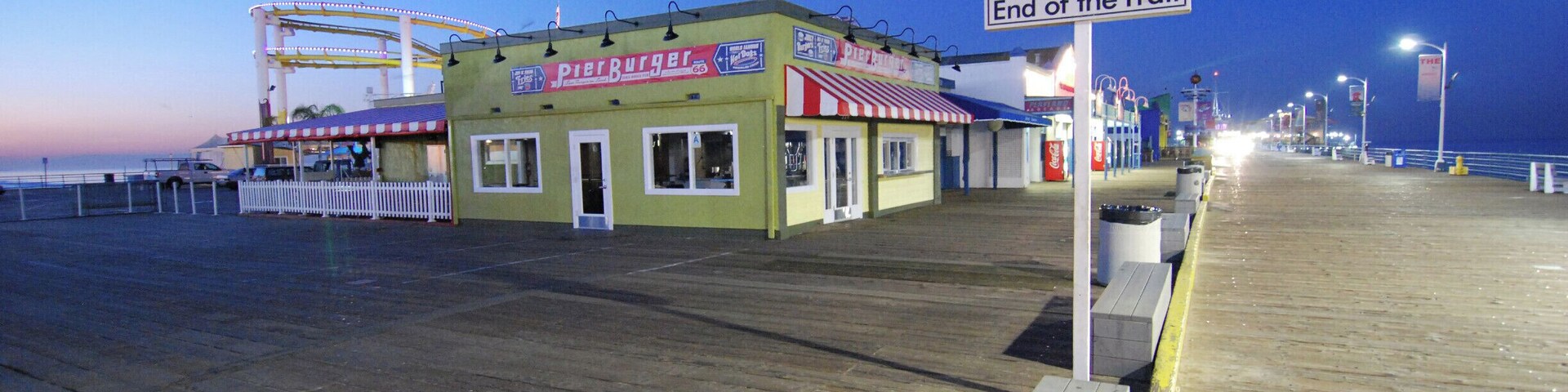 Um calçadão com um restaurante chamado 'SANTA MONICA 66' e uma placa indicando 'Fim da Trilha'.