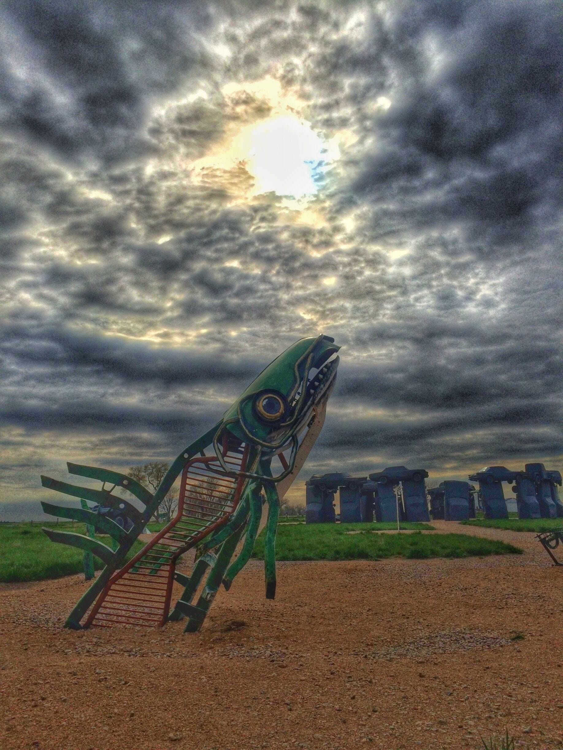 Escultura de peixe em um parque sob um céu nublado.