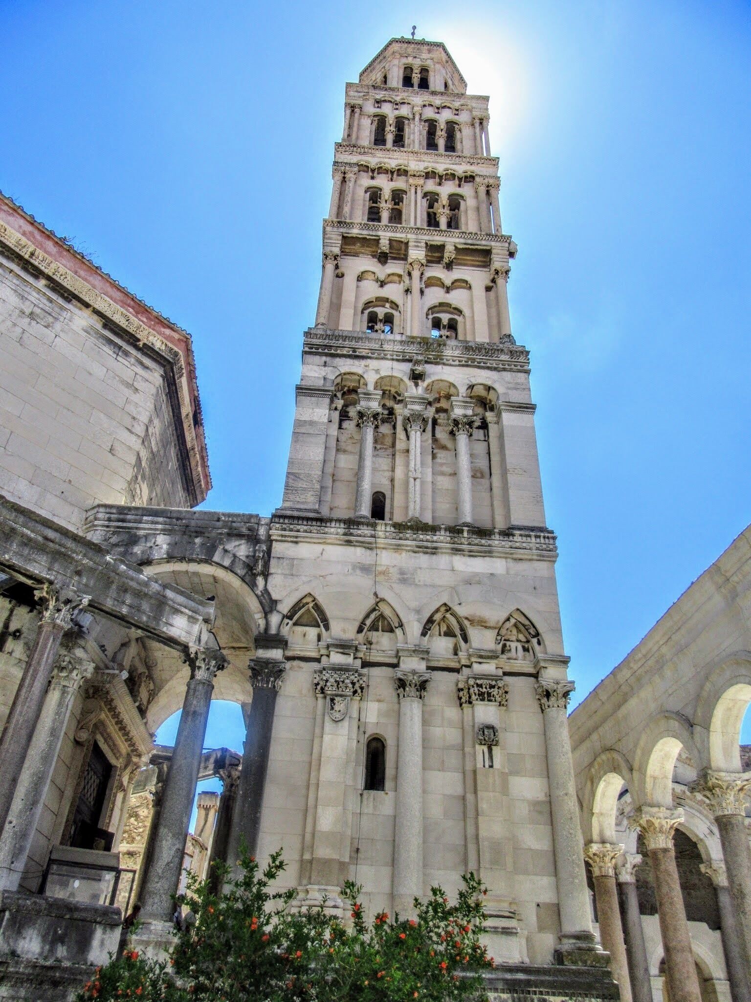 Uma torre alta e ornamentada, com várias arcos e colunas, cercada por arquitetura clássica.