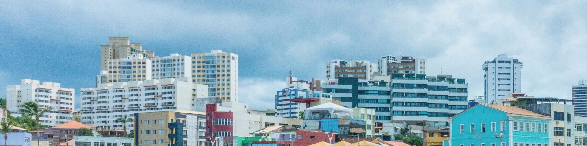 Paisagem costeira com edifícios coloridos, uma praia de areia e barcos na água.