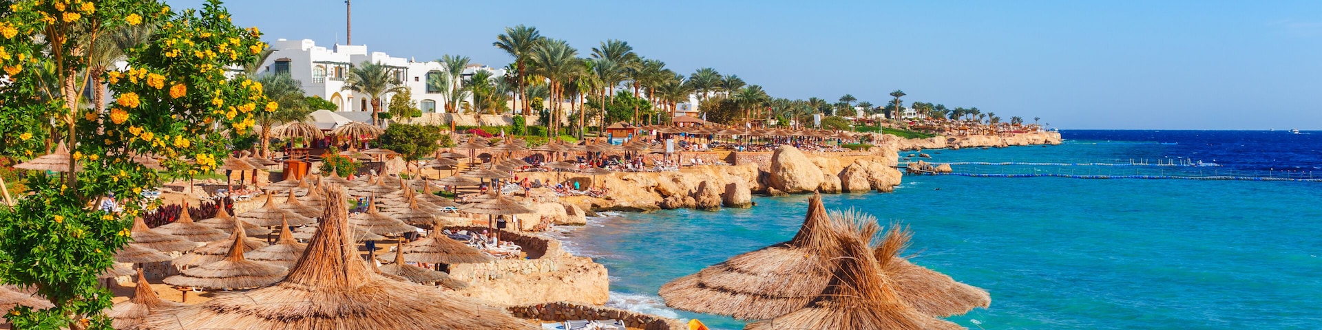 Um resort costeiro com guarda-sóis de palha, cadeiras de praia e um mar azul cristalino.
