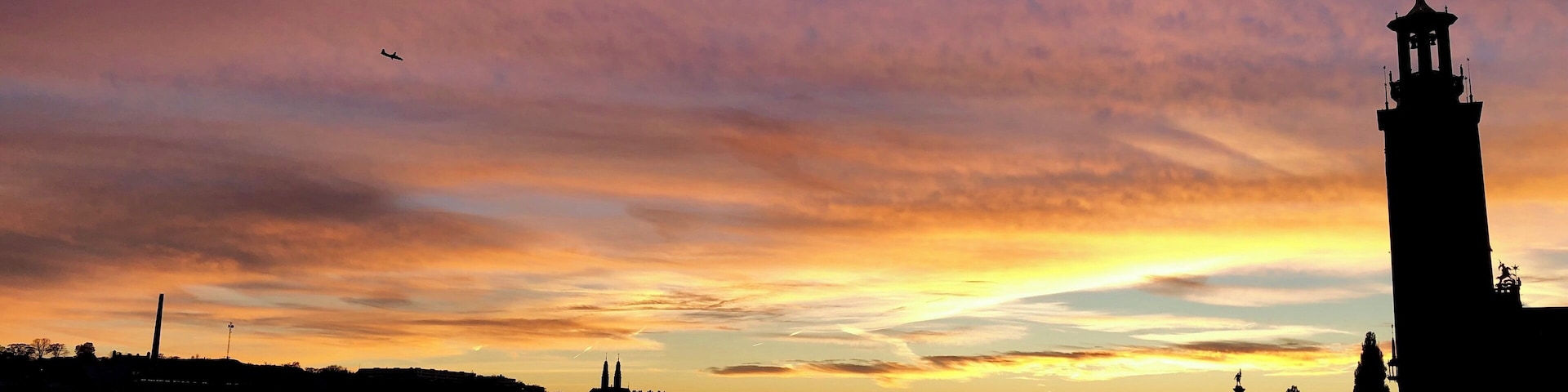 Um pôr do sol sobre a água, com uma torre e duas torres pontiagudas recortadas no céu.