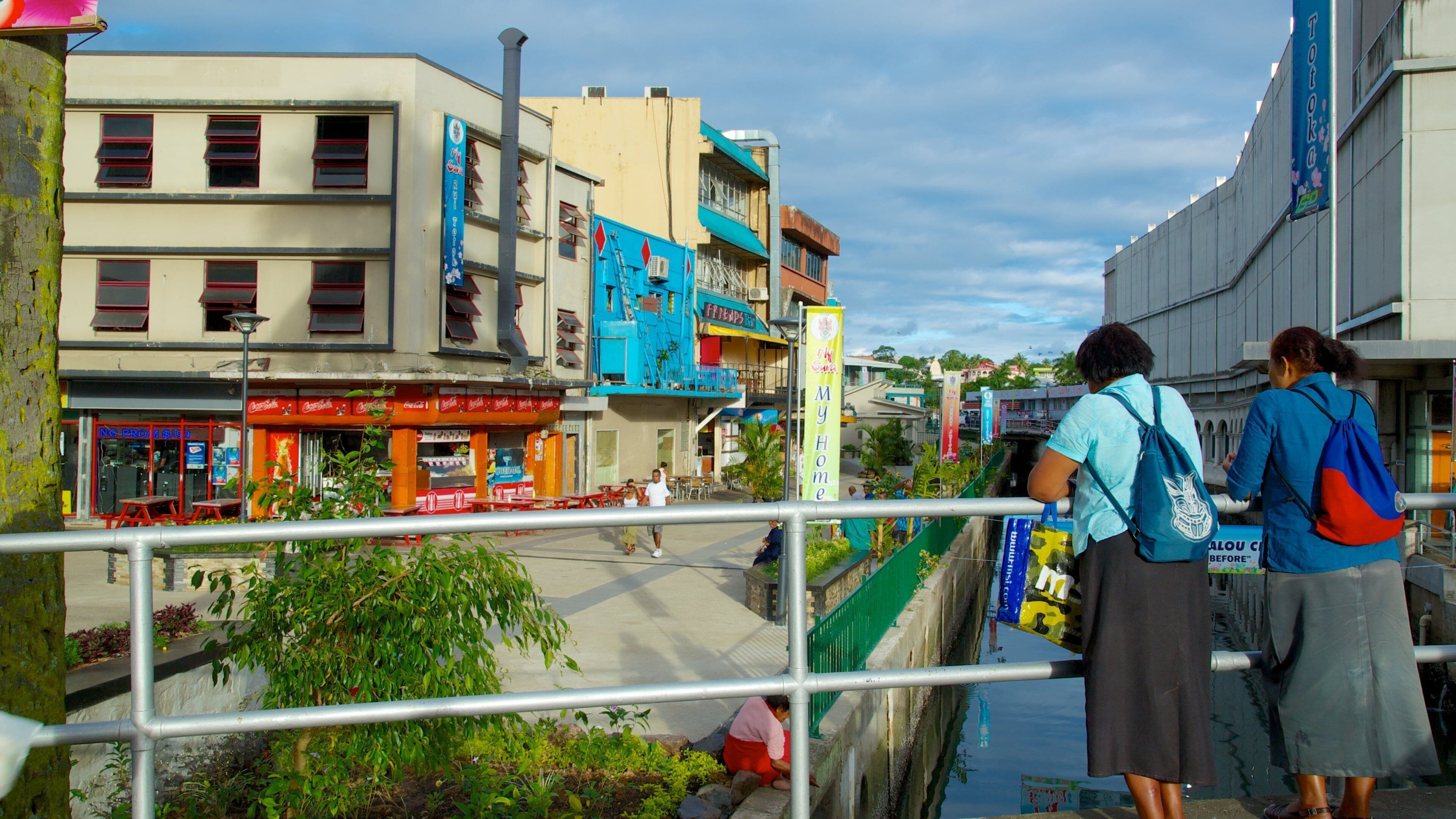 Paisagem urbana com mistura de arquitetura moderna e tradicional, incluindo uma loja Coca-Cola e um edifício com fachada azul.