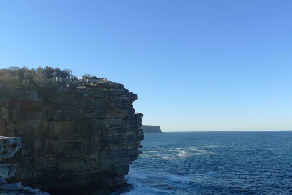 Um penhasco costeiro com ondas quebrando e um céu azul límpido.