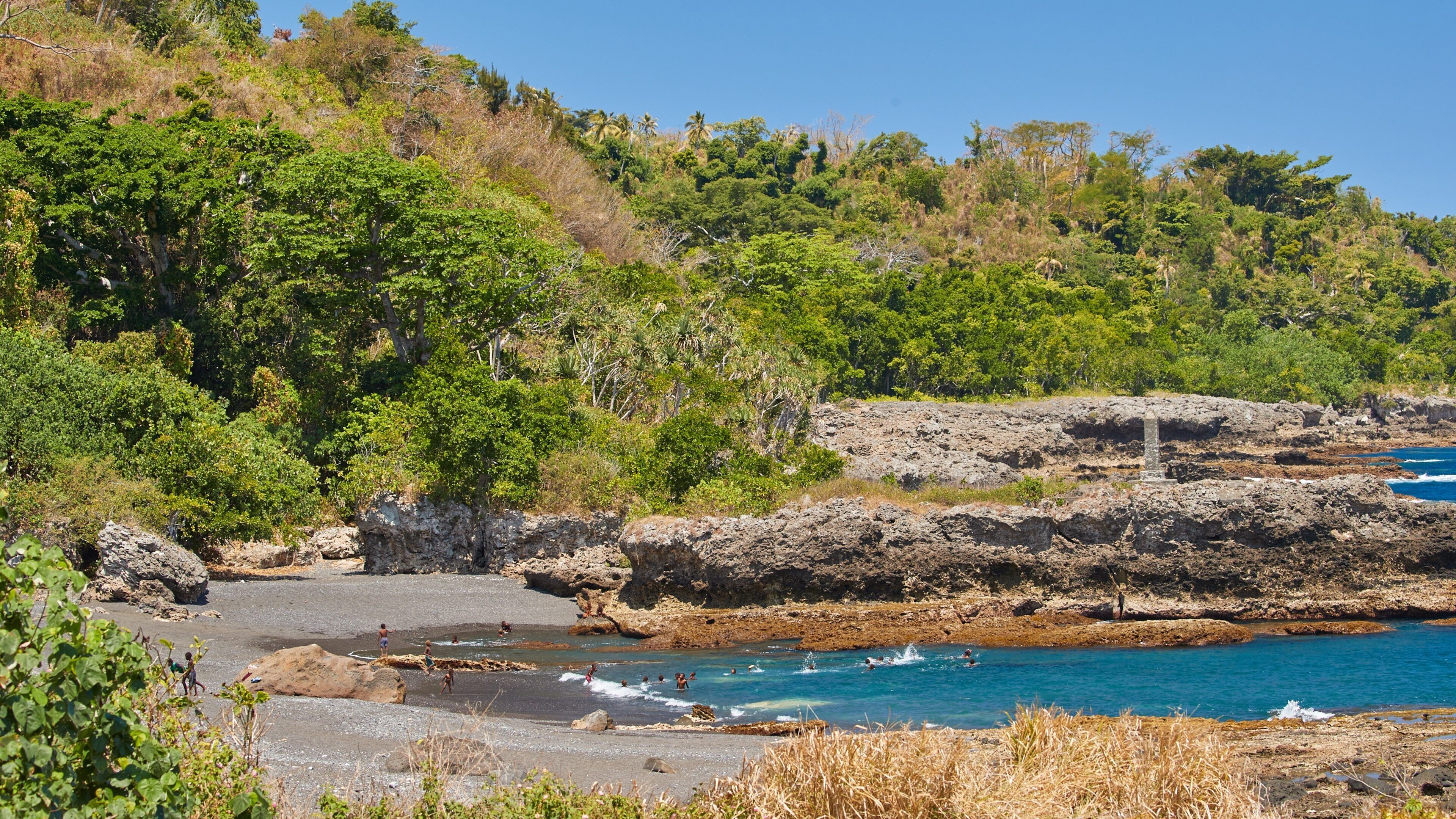Paisagem costeira com costas rochosas, água azul cristalina e vegetação verde exuberante.