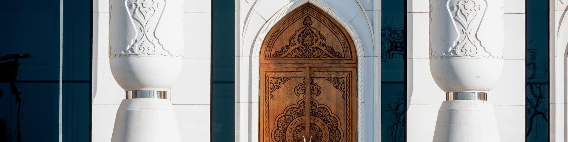 Um edifício com colunas brancas, uma porta de madeira com esculturas detalhadas e uma parede azul.