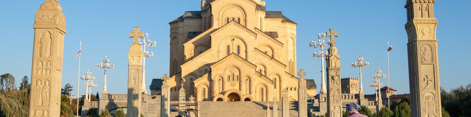 Uma igreja grande com uma cúpula imponente e várias cruzes, rodeada por monumentos de pedra e um céu limpo.