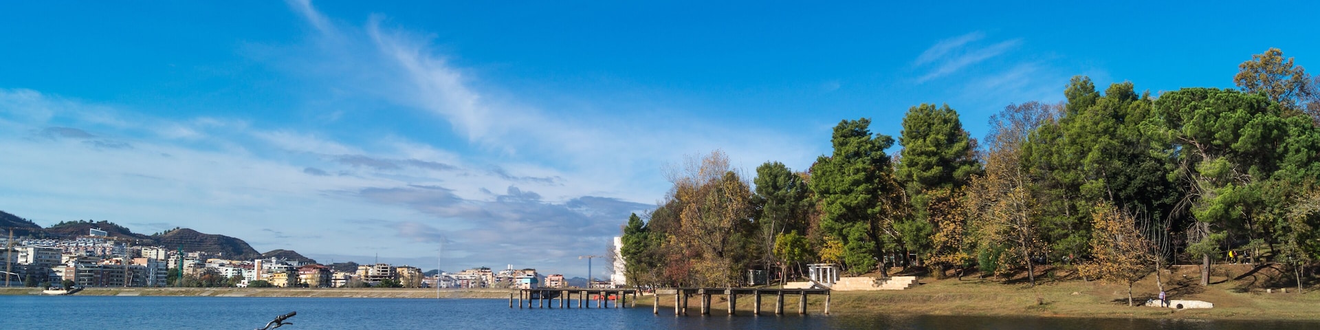 Um lago com um cais, uma bicicleta e um horizonte urbano ao fundo.