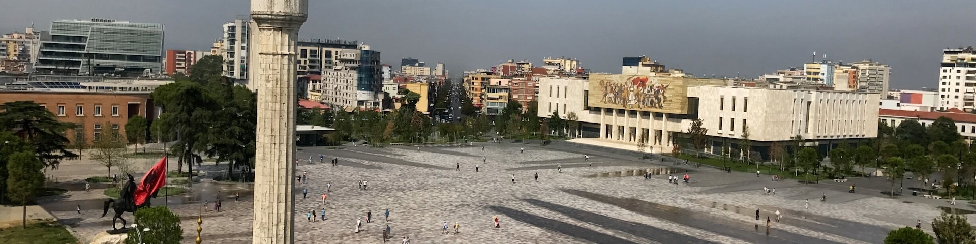 Uma grande praça aberta com um minarete imponente, rodeada por edifícios modernos e uma estrutura em forma de cúpula.