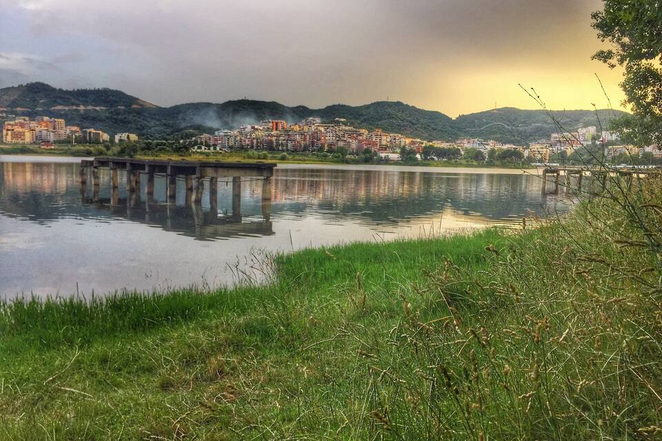 Um lago com um cais, uma paisagem urbana ao fundo e colinas.