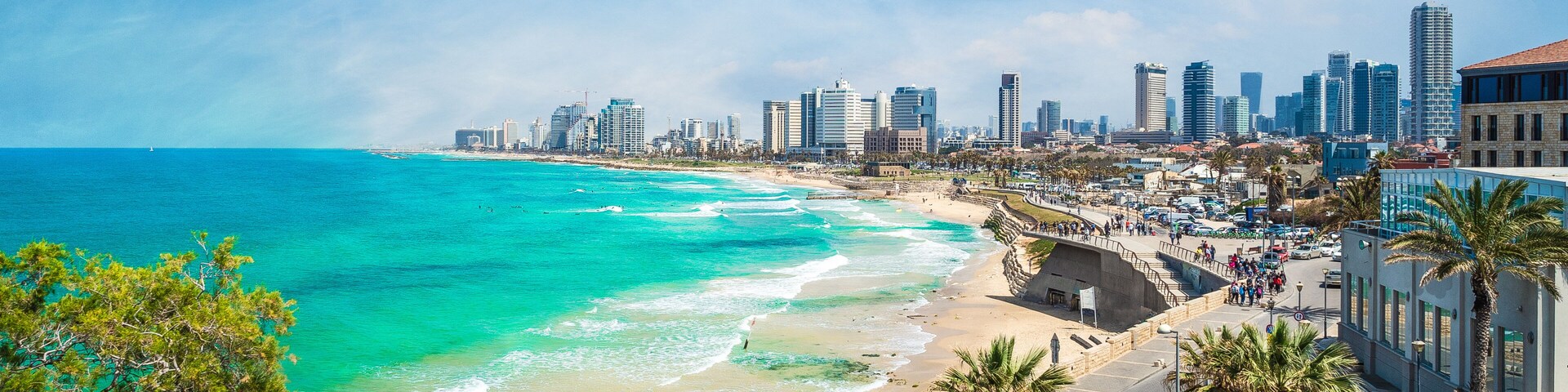 Paisagem costeira com praia, palmeiras e arranha-céus.