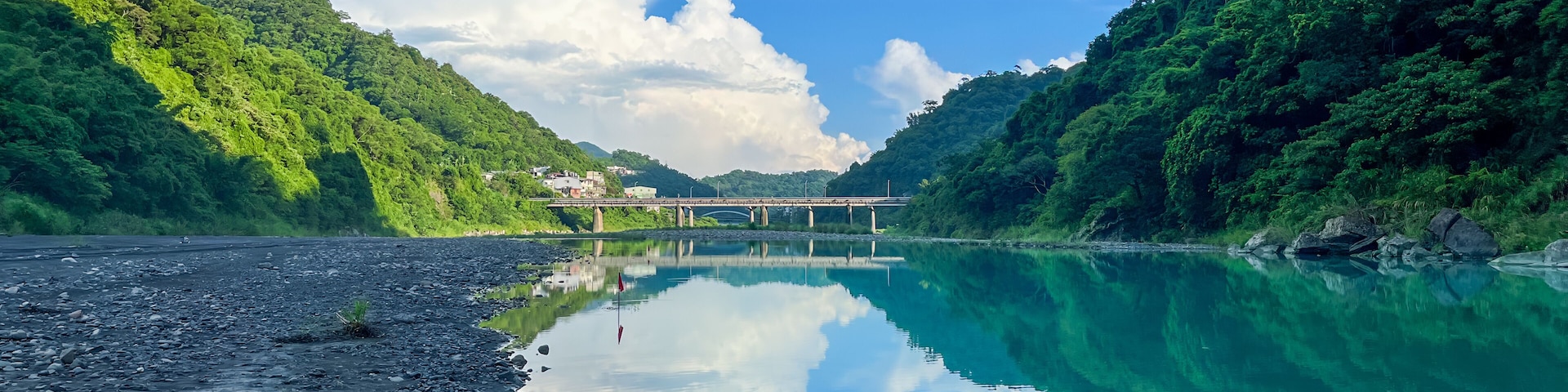 Um rio com uma ponte, rodeado por colinas verdes exuberantes.