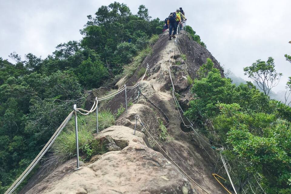 Trilha rochosa na montanha com uma escada de corda e caminhantes no cume.
