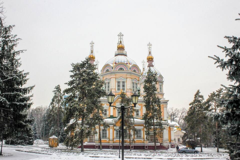 Um edifício coberto de neve com cúpulas ornamentadas e uma cúpula central, cercado por árvores.