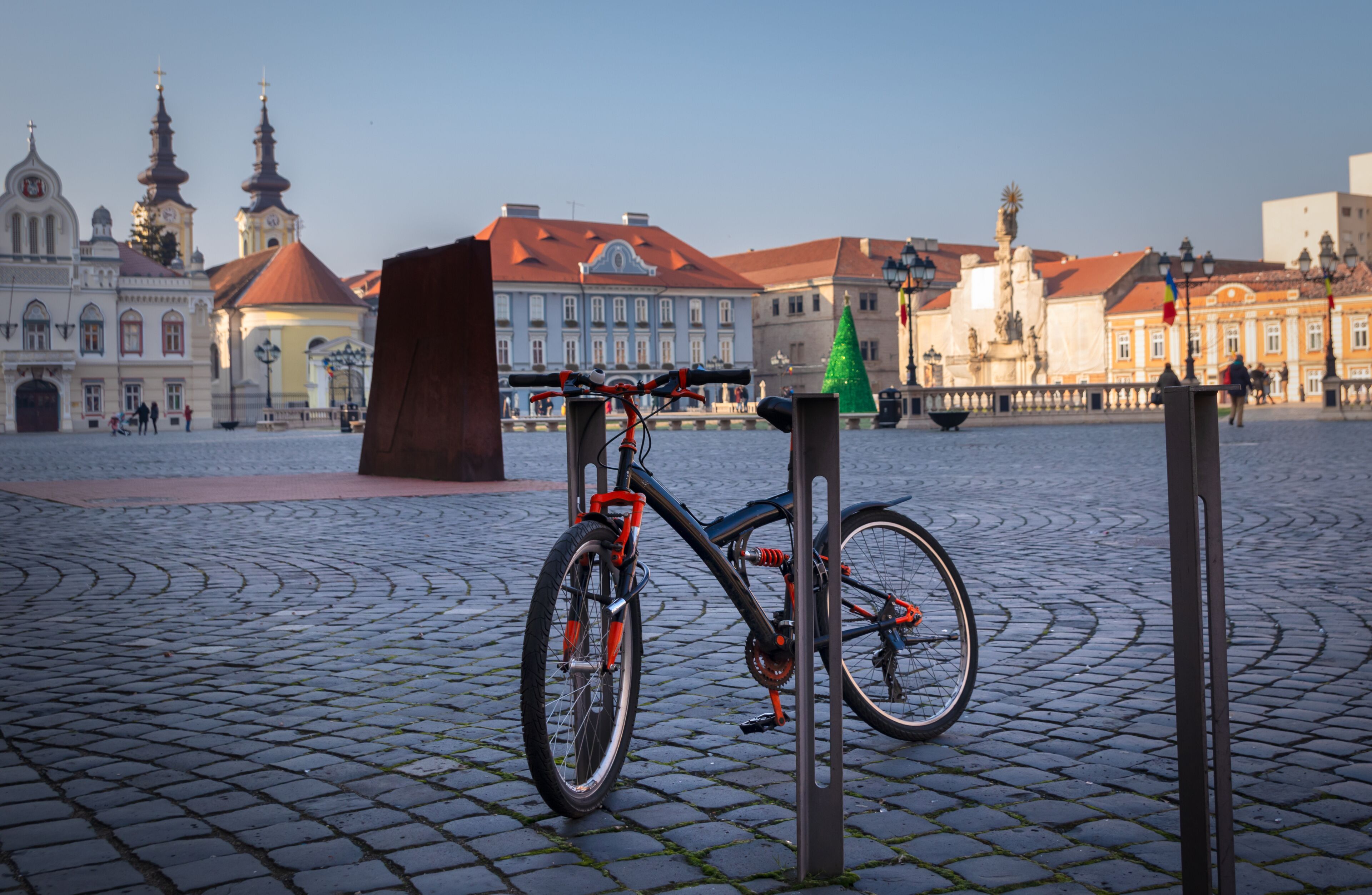 Uma bicicleta estacionada em calçada de paralelepípedos, com edifícios históricos e uma igreja ao fundo.