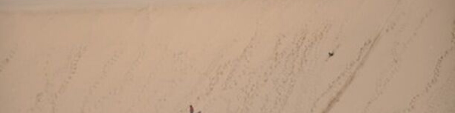 Uma duna de areia grande com pegadas e algumas pessoas caminhando.