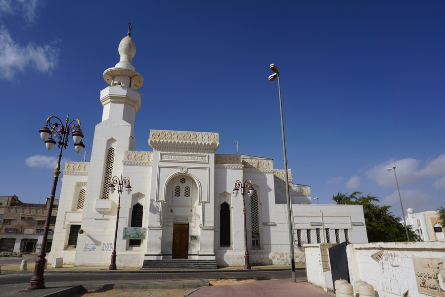 Uma mesquita branca com um minarete, janelas em arco e uma porta de madeira.