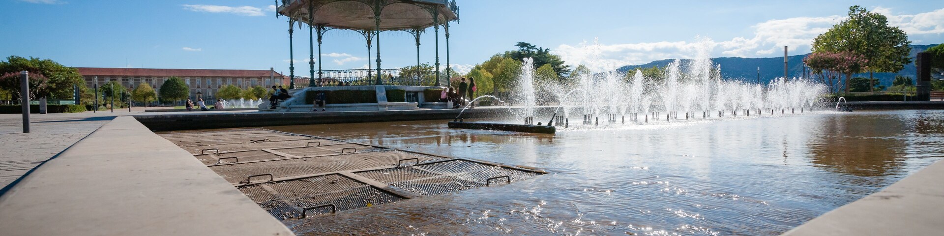 Uma fonte com jatos de água, um gazebo e um céu azul límpido.
