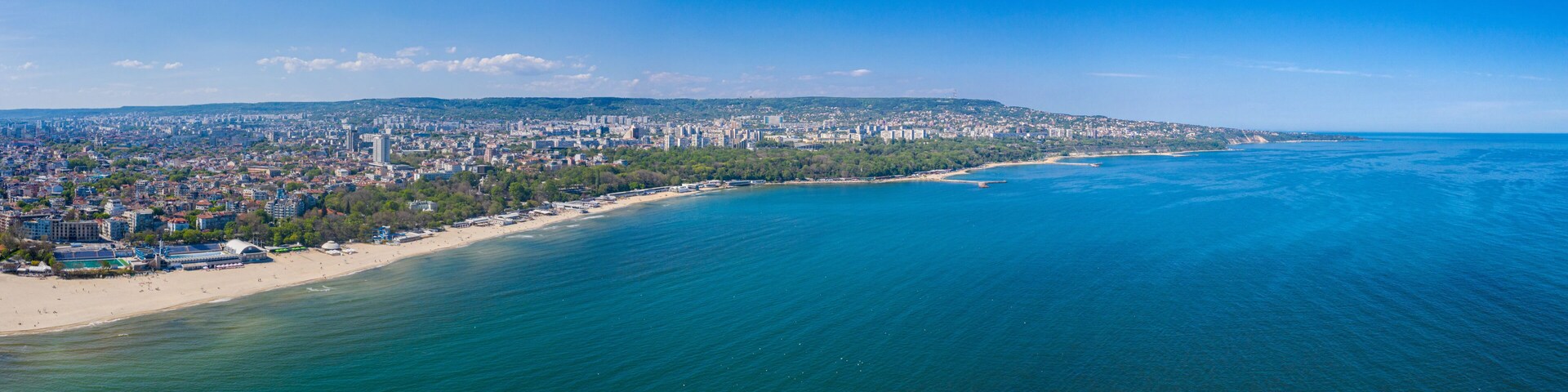 Paisagem costeira com praia, área urbana densa e uma colina ao longe.