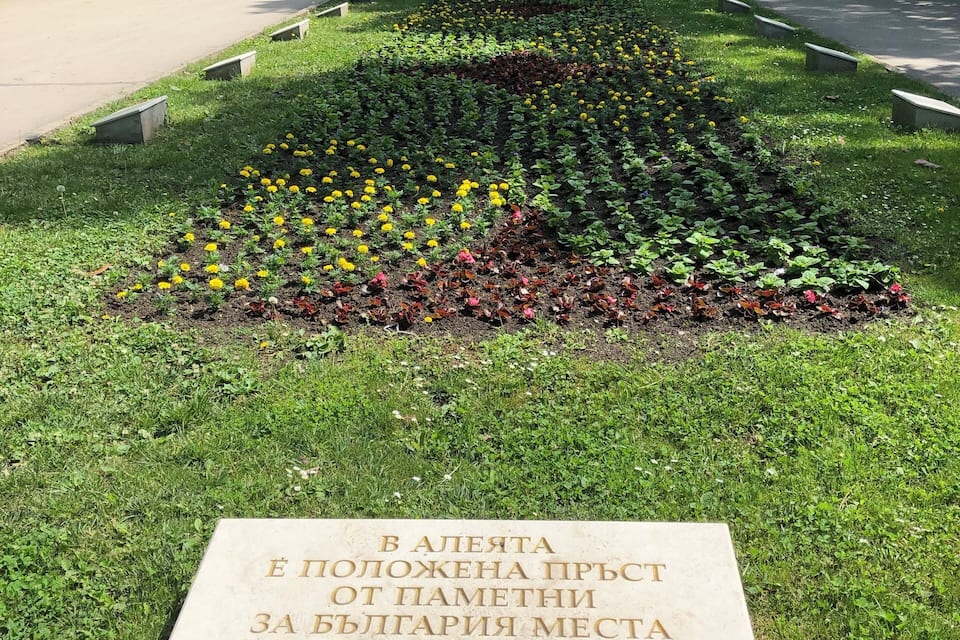 Um parque com um canteiro de flores central e uma placa com texto em língua estrangeira.