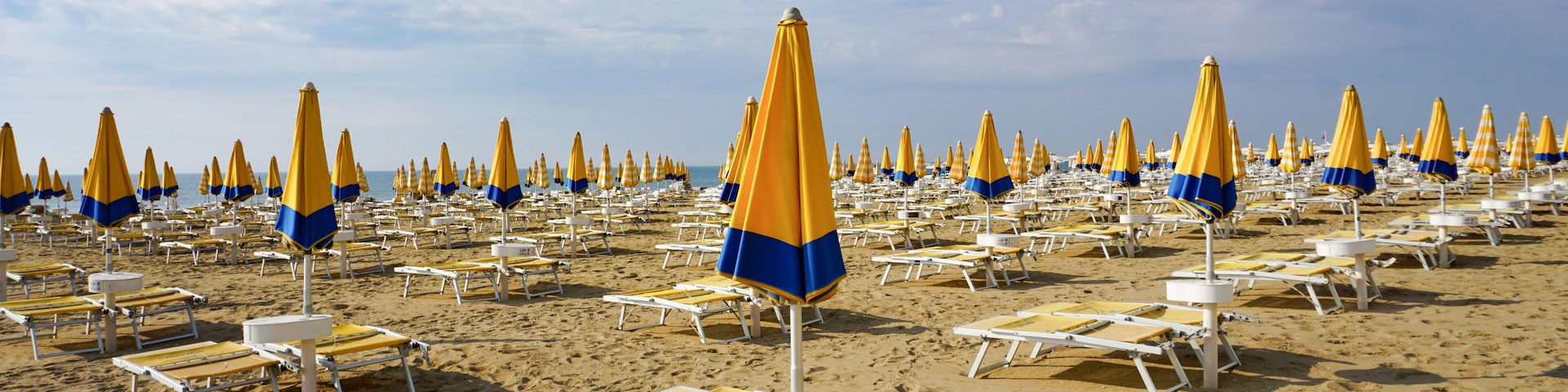 Uma praia com fileiras de espreguiçadeiras e guarda-sóis amarelos e azuis.