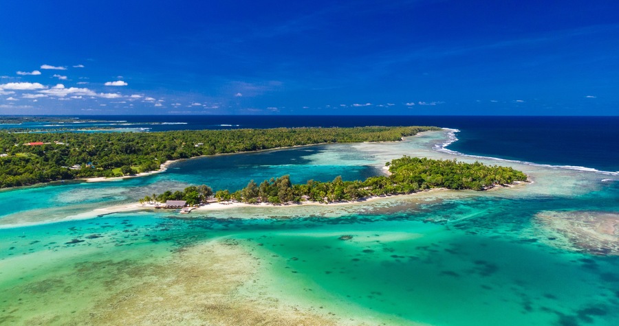 Ilha tropical com águas turquesa cristalinas, vegetação verde exuberante e uma praia arenosa.