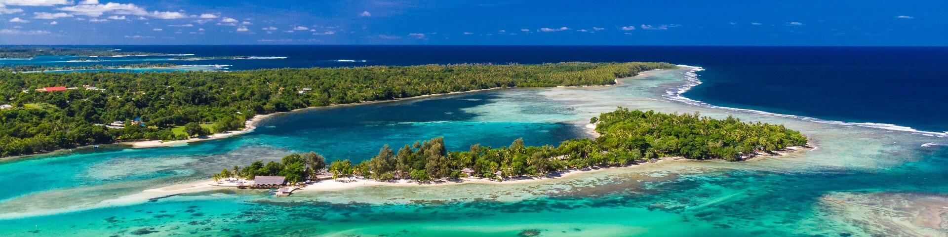 Ilha tropical com águas turquesa cristalinas, vegetação verde exuberante e uma praia arenosa.