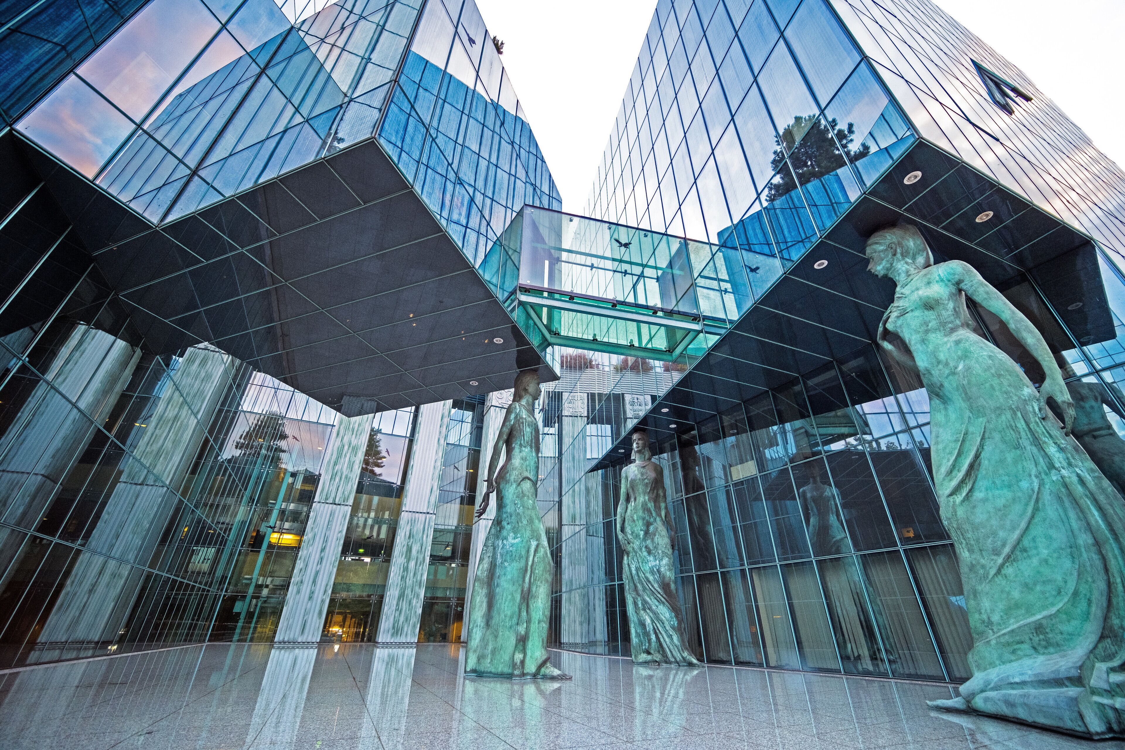 Um edifício moderno de vidro com superfícies refletoras e estátuas de bronze de mulheres.