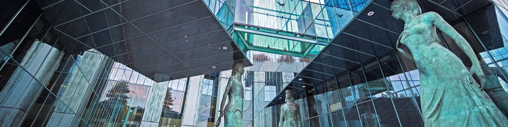 Um edifício moderno de vidro com superfícies refletoras e estátuas de bronze de mulheres.