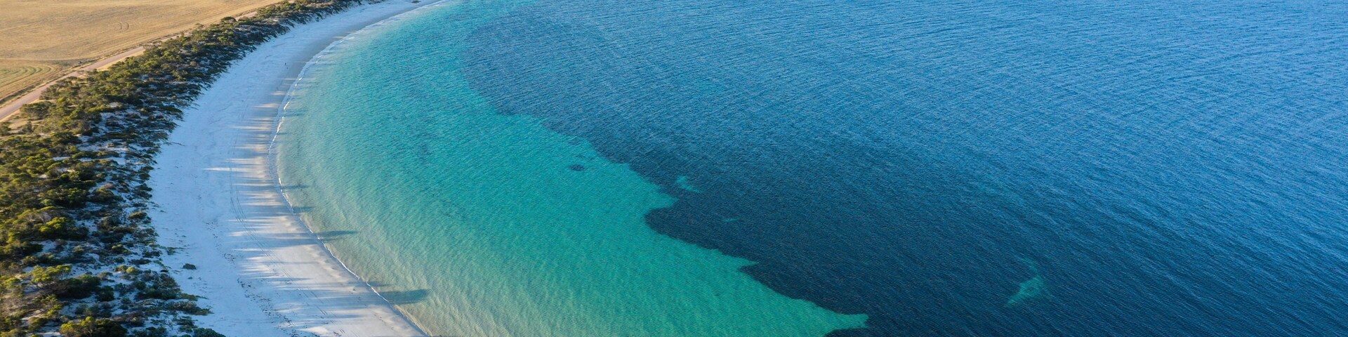 Paisagem costeira com uma praia arenosa, águas turquesa cristalinas e uma linha de costa distante.