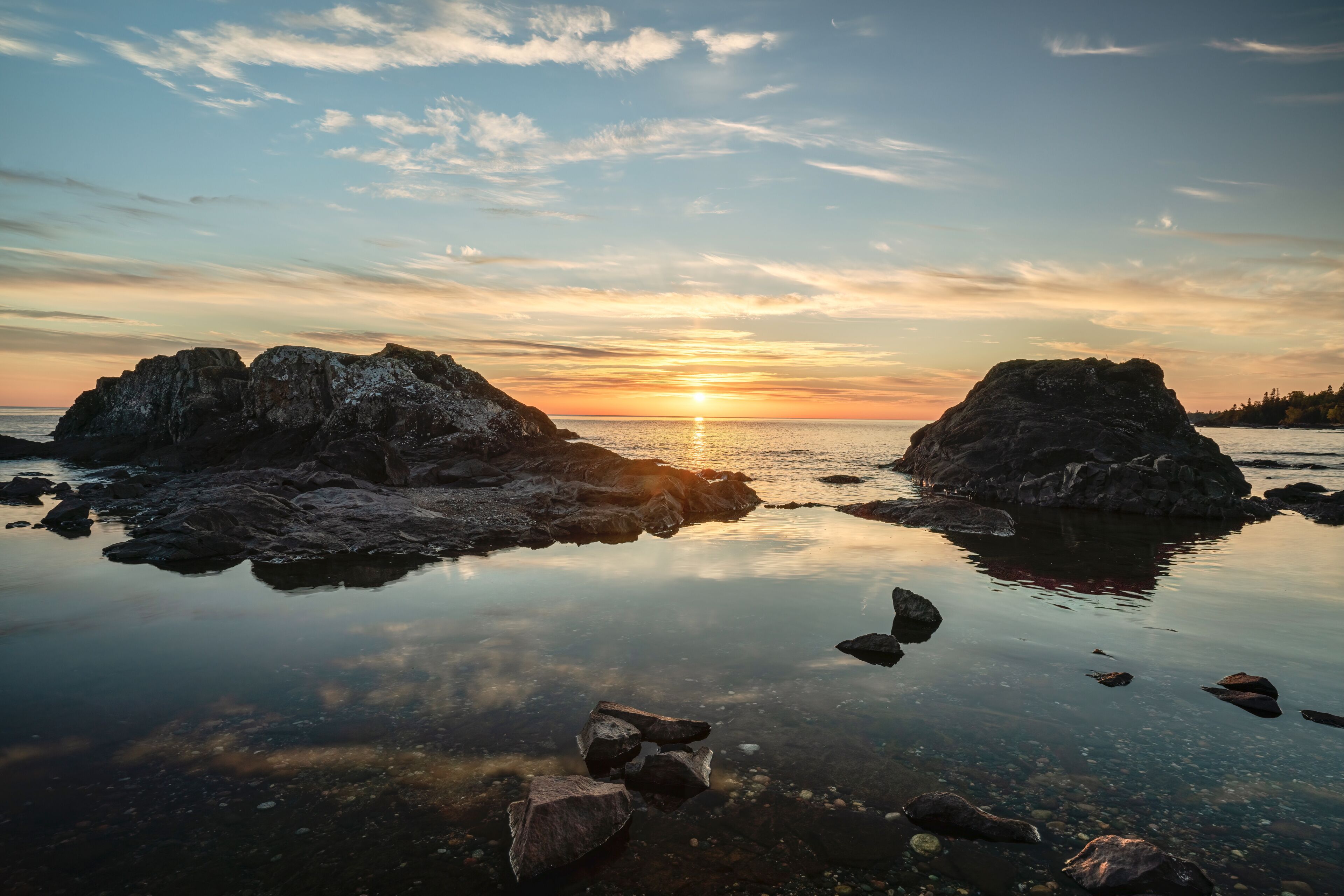 Pôr do sol sobre um mar calmo, com duas formações rochosas em destaque ao primeiro plano.