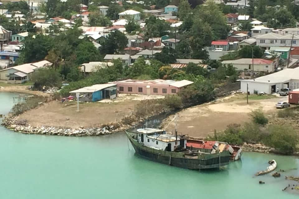Uma vila costeira com um barco ancorado perto da praia, rodeada por edifícios residenciais e vegetação.