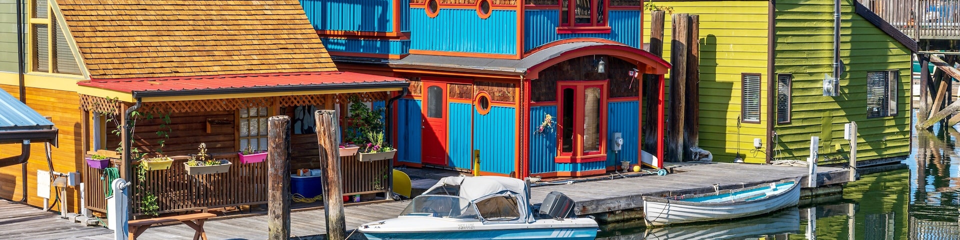 Casas de madeira coloridas à beira de um canal tranquilo com barcos atracados.