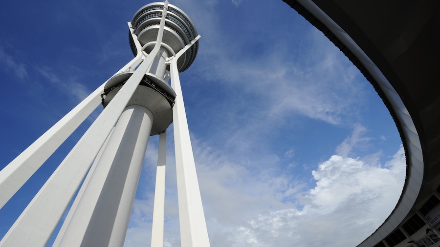 Uma torre com elementos estruturais brancos e um deque circular de observação contra um céu azul com nuvens.