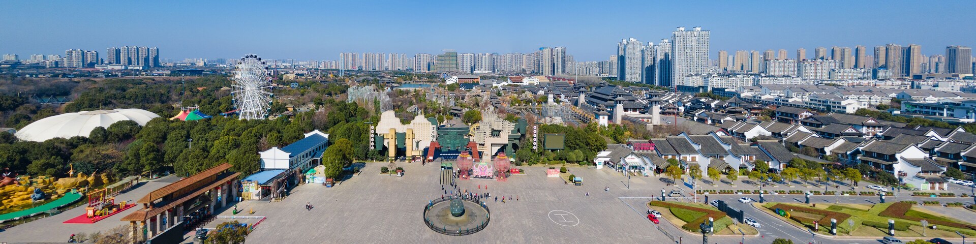 Vista aérea de uma cidade com uma grande praça aberta, uma roda gigante, edifícios tradicionais e modernos apartamentos altos.