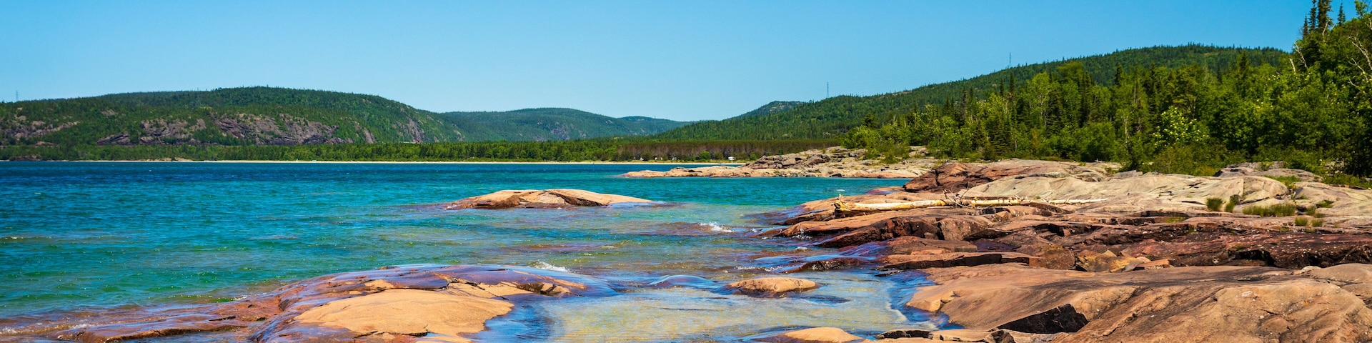Uma costa rochosa com águas turquesa cristalinas, cercada por colinas verdejantes e uma floresta densa.