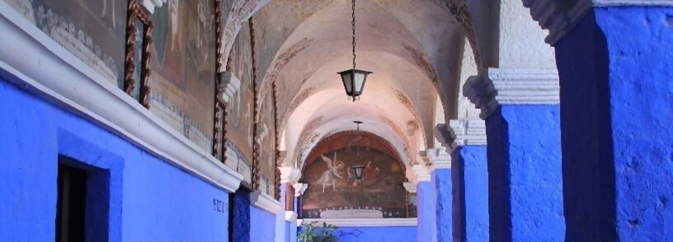 Um corredor com paredes azuis, tetos em arco e um candeeiro pendente.
