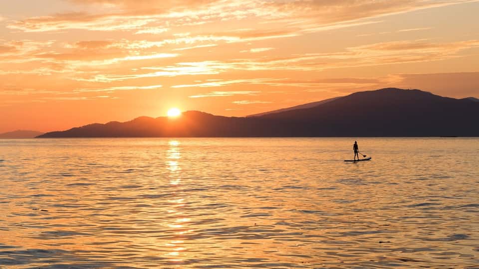 Um pôr do sol sobre um mar calmo com a silhueta de alguém praticando paddleboarding.