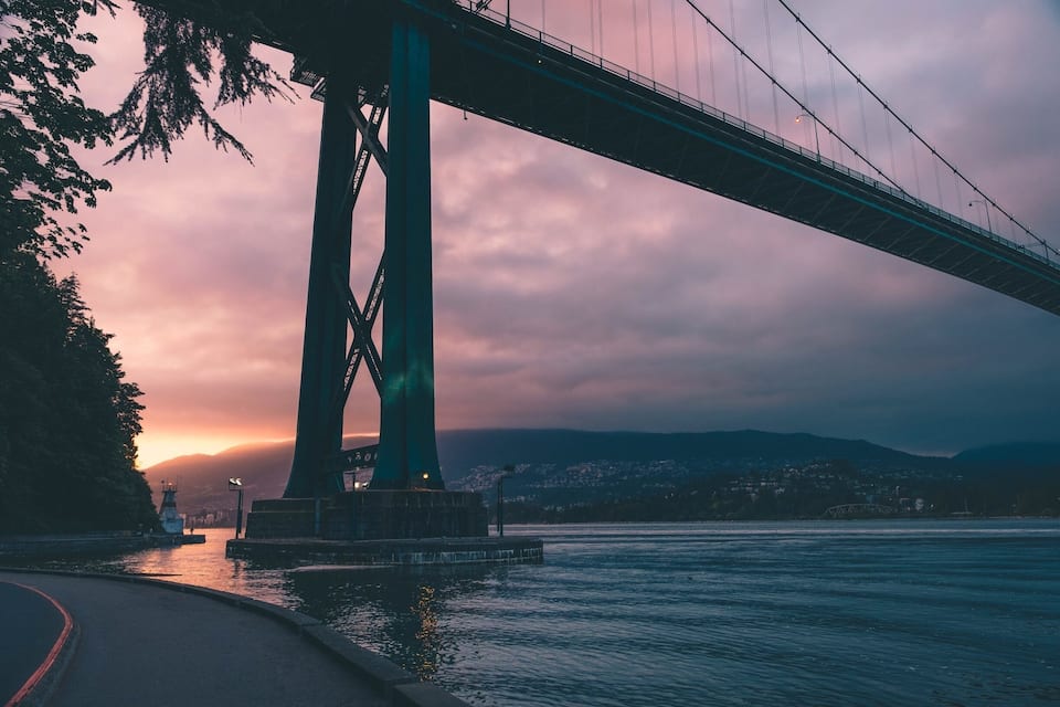 Uma ponte com dois pilares imponentes, um pôr do sol ao fundo e um corpo de água.