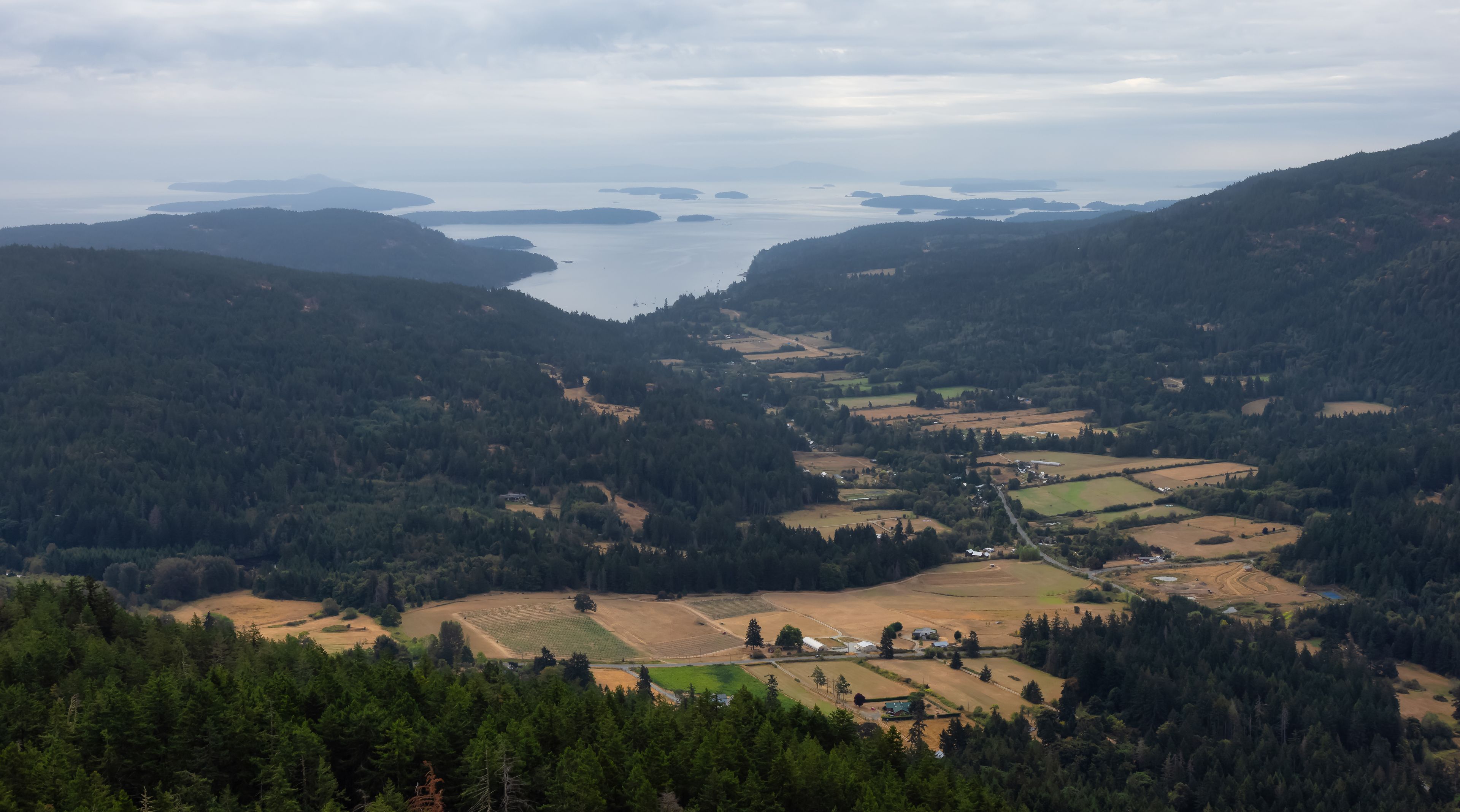 Paisagem montanhosa com um vale, campos e um corpo d'água.