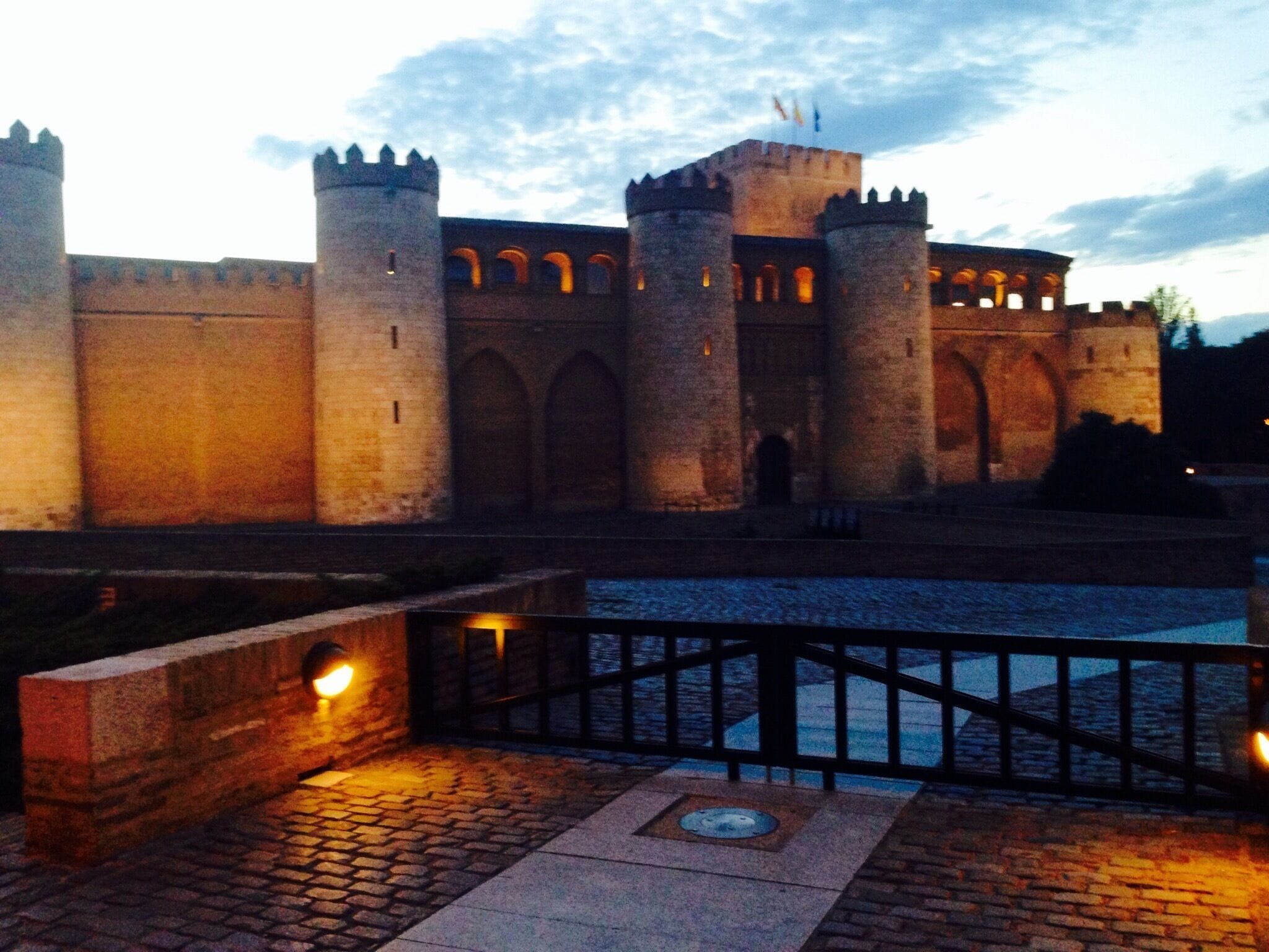 Um castelo histórico com múltiplas torres e janelas em arco, um caminho de calçada e uma entrada com portão.