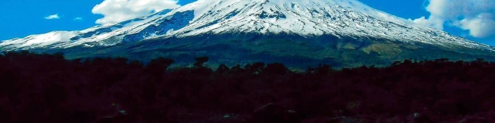 Montanha coberta de neve com um rio em primeiro plano.