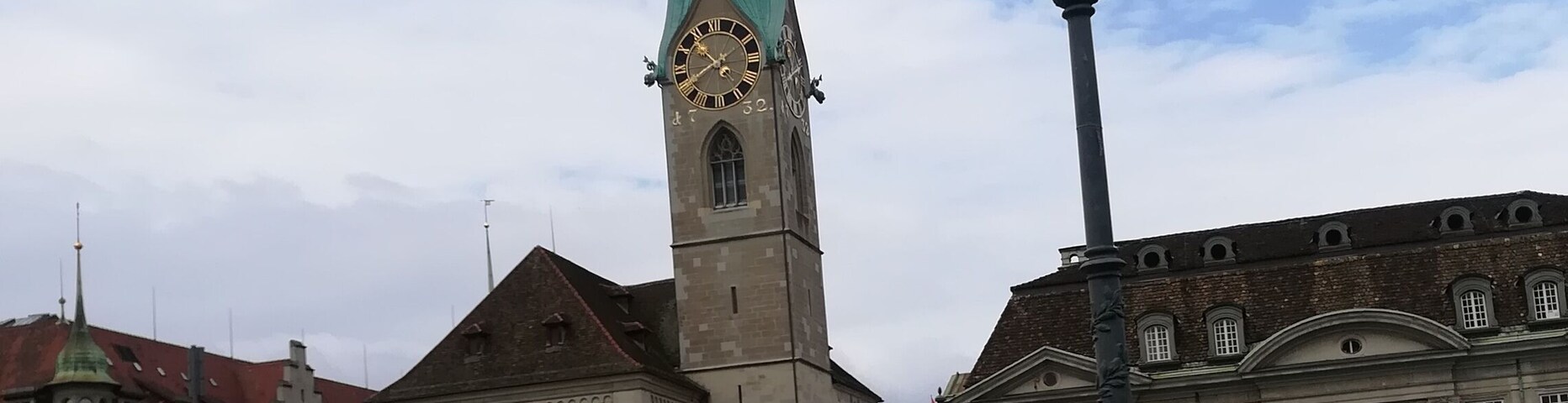 Uma igreja histórica com uma torre alta e relógio, uma ponte com pedestres e um rio.