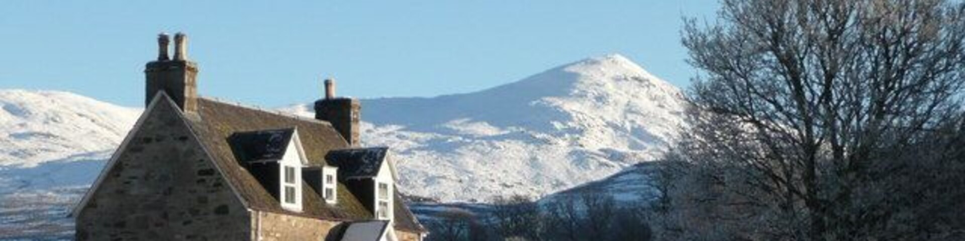 Uma casa de pedra com paisagem coberta de neve e uma montanha ao fundo.